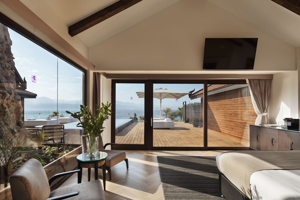 Quarto de hotel moderno com uma grande porta de vidro deslizante que dá para uma varanda com vista para o oceano.