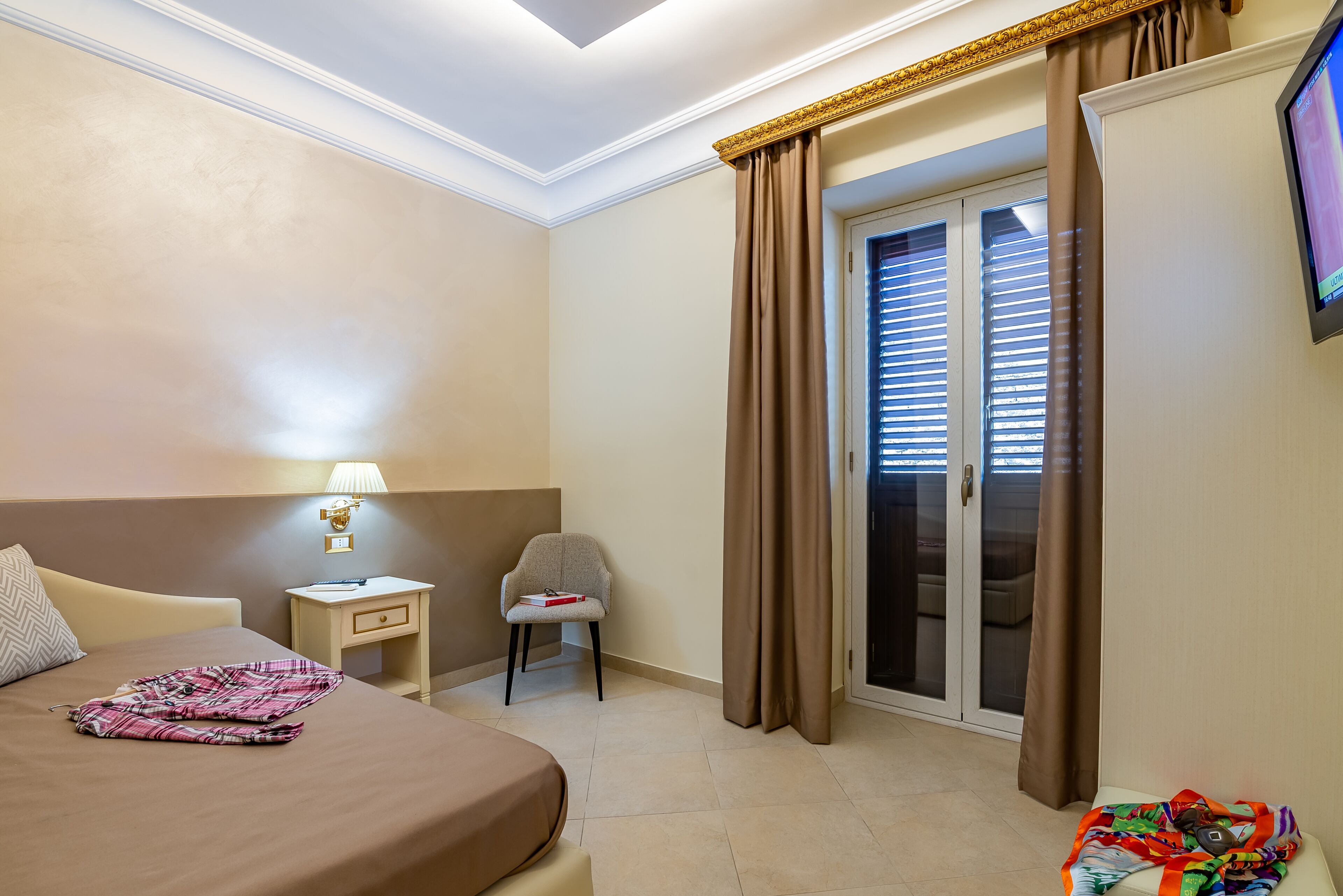 Quarto de hotel com cama, uma cadeira, mesa de cabeceira, abajur e porta de vidro deslizante.