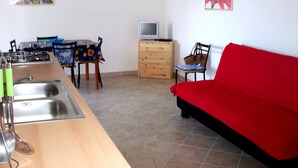 Espaço compacto com cozinha compacta, área de refeições, sofá vermelho, televisão e uma obra de arte floral na parede.