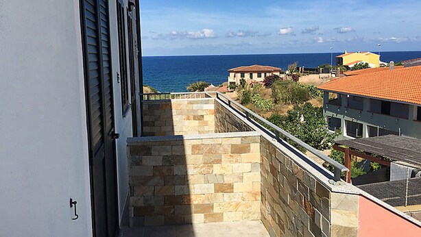 Varanda com parede de pedra e vista para o mar e edifícios próximos.