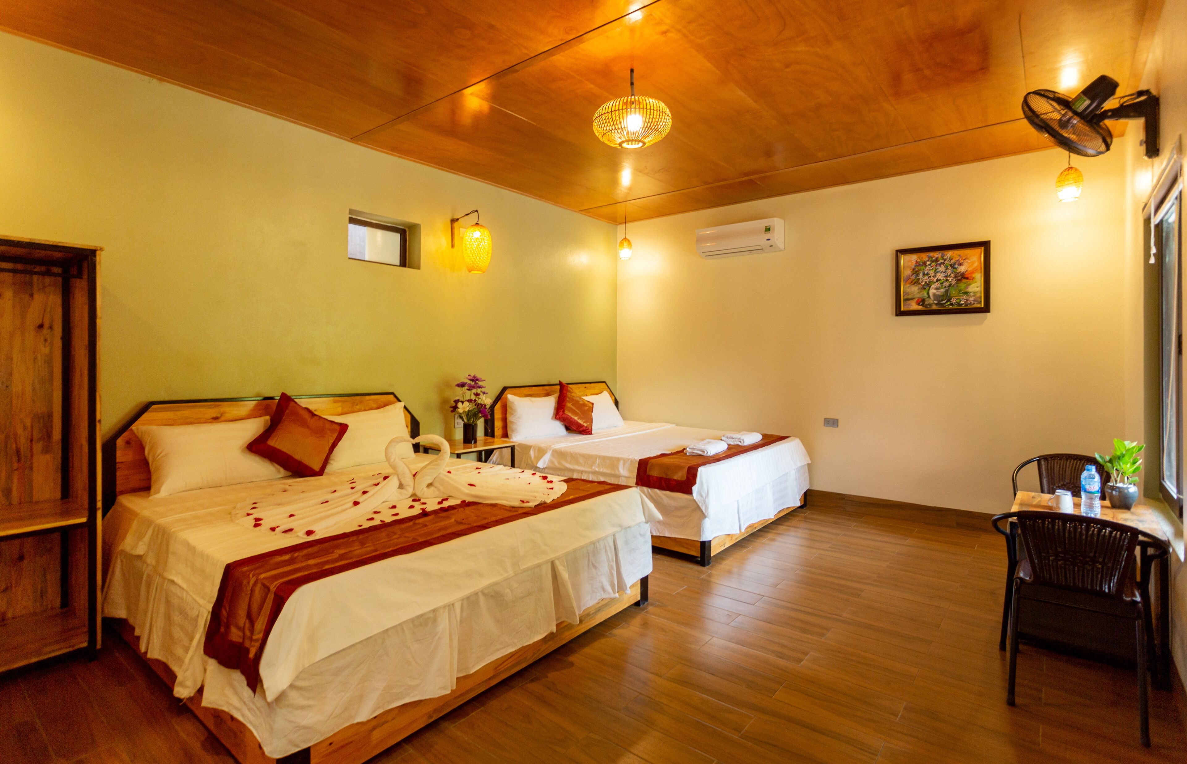 Quarto de hotel com duas camas, piso de madeira, uma mesa de jantar com cadeiras e uma janela com vista.