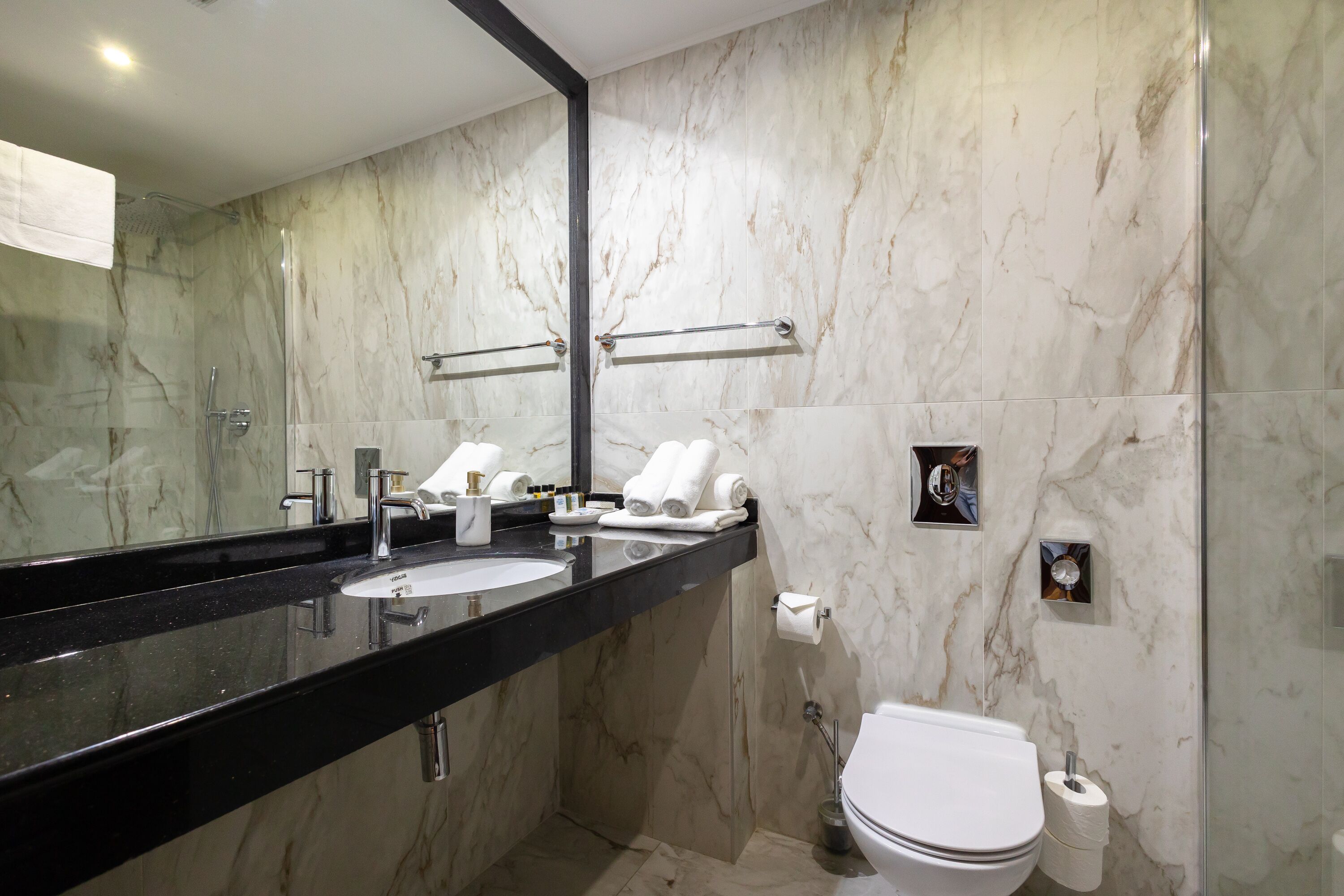 Casa de banho moderna com bancada preta, lavatório branco, espelho grande e sanita.