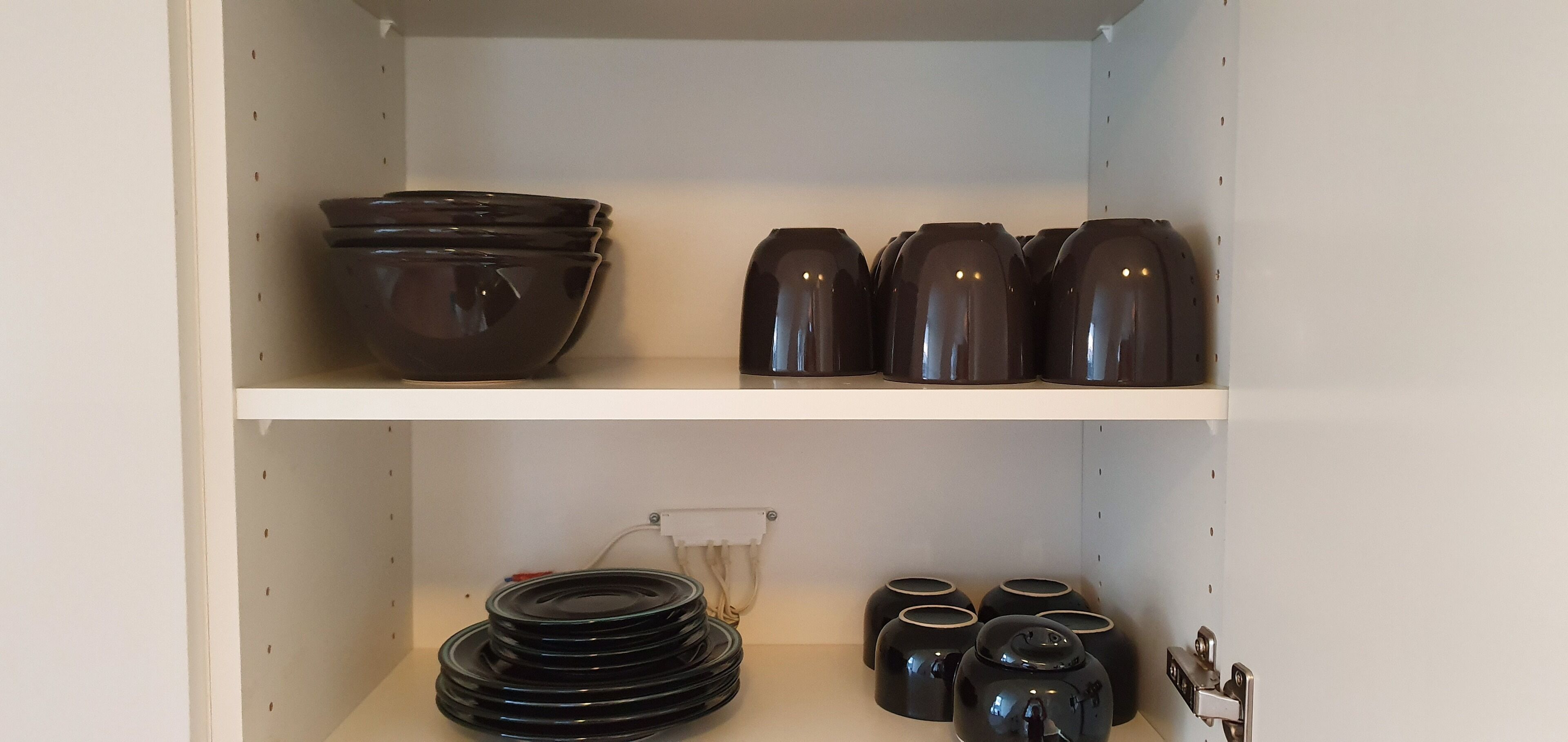Uma prateleira com tigelas pretas, vasos e cabos pretos enrolados.