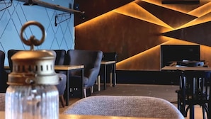 Um interior moderno com um design geométrico na parede, uma área de refeições com mesas e cadeiras, e uma televisão em um móvel.