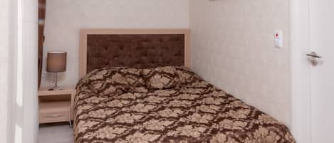 Quarto com cama, mesa de cabeceira, luminária, ar condicionado e porta.