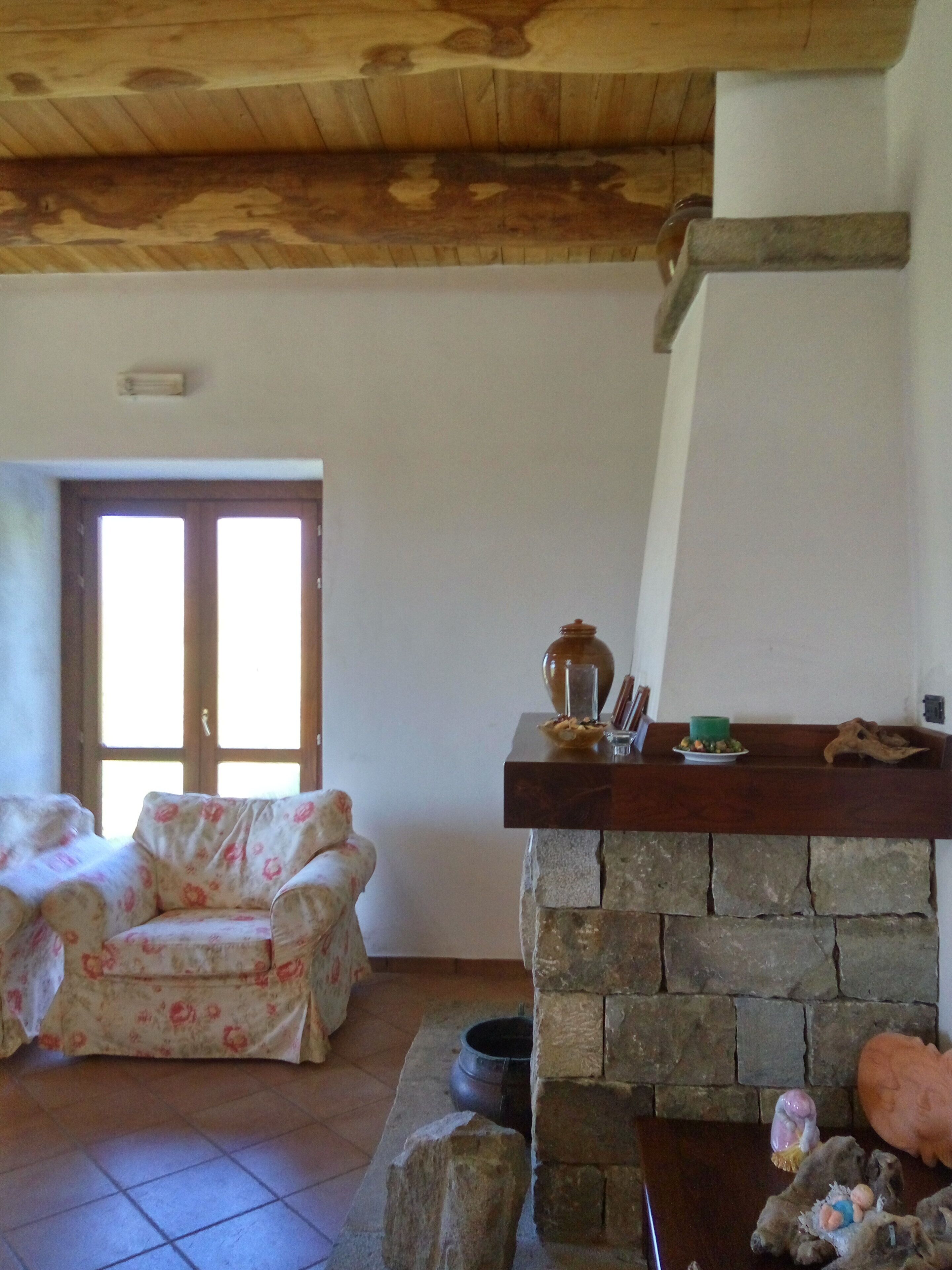 Uma sala de estar acolhedora com teto de madeira, lareira de pedra, sofá estampado e uma porta que dá para o exterior.