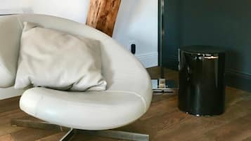 Uma sala de estar moderna com um sofá de couro branco, uma viga de madeira, um abajur preto e uma lixeira preta.