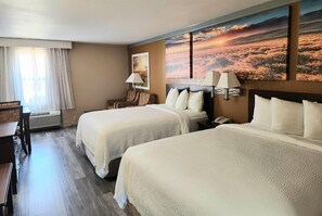 Quarto de hotel com duas camas, uma escrivaninha, uma cadeira, um abajur e um quadro grande na parede.