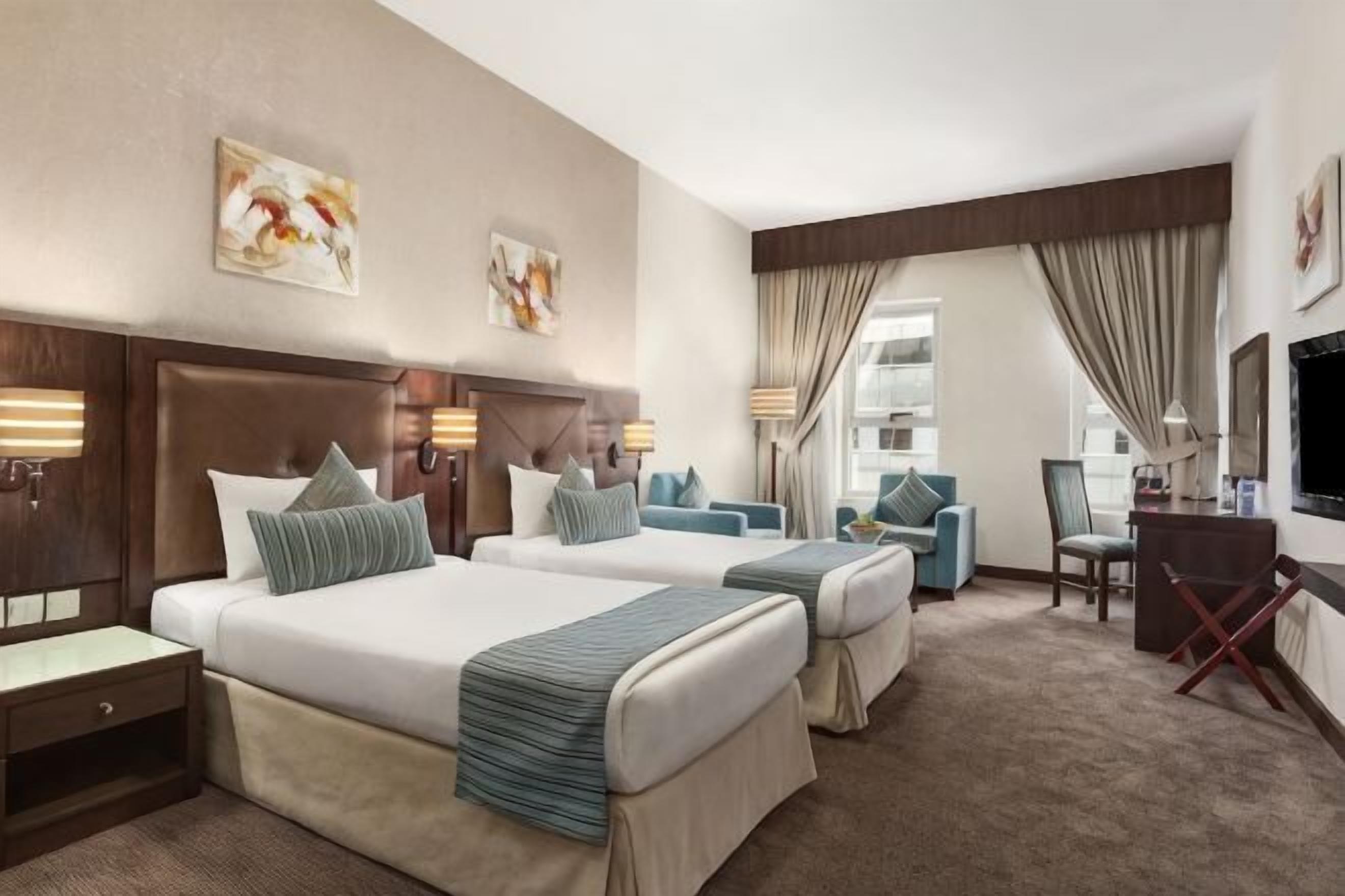 Quarto de hotel com duas camas, uma escrivaninha, uma cadeira e uma televisão.