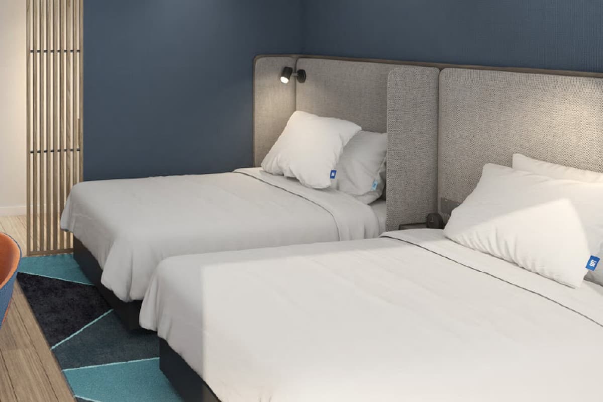 Quarto de hotel com duas camas, uma cadeira e piso de madeira.