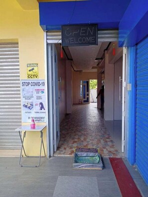 Um corredor com uma placa indicando 'OPEN WELCOME' e outra placa com informações sobre medidas de segurança COVID-19.