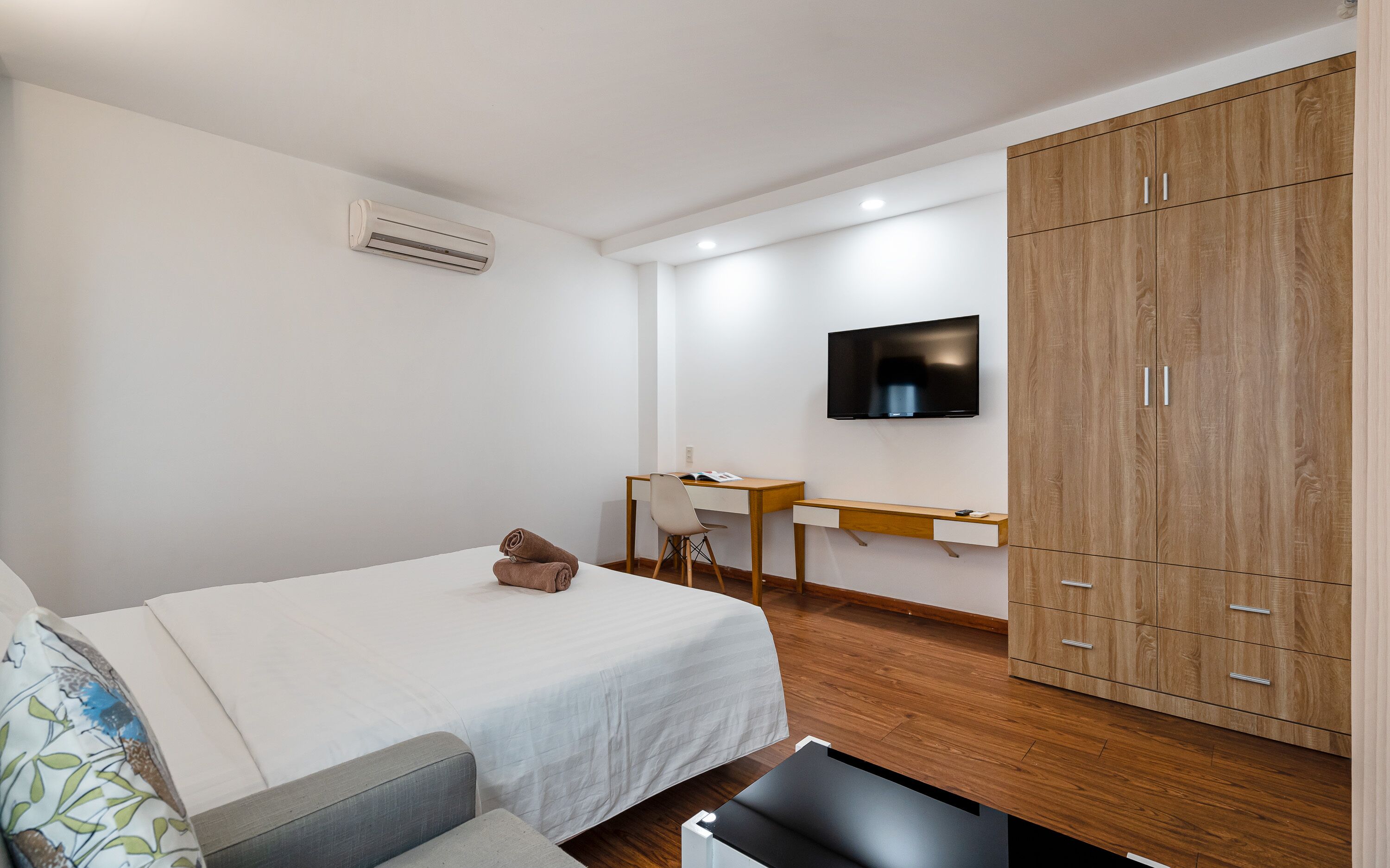Quarto de hotel com cama, escrivaninha, cadeira, televisão e guarda-roupa.