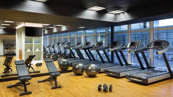 Uma academia com esteiras, bolas de exercício e halteres.