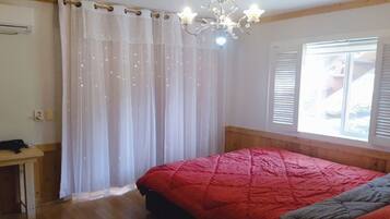 Quarto com colcha vermelha, cabeceira de madeira, cortina branca e lustre.