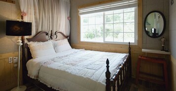 Um quarto com uma cama de madeira, uma mesa de cabeceira, um espelho e uma janela com cortinas.