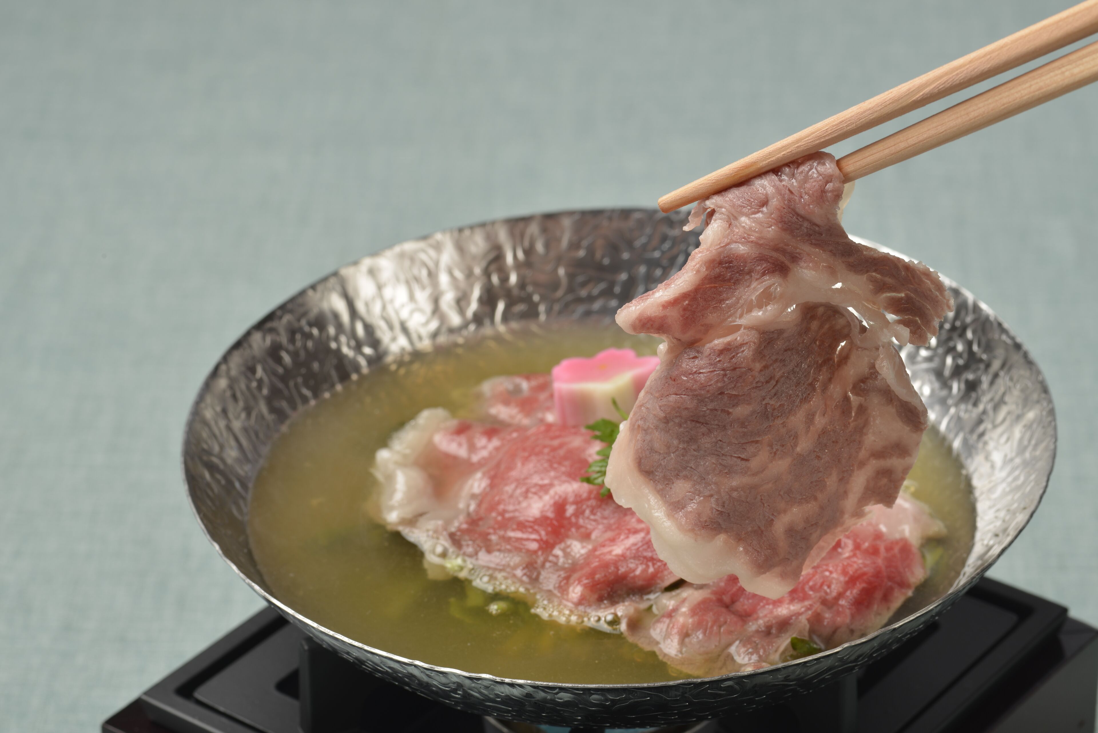 Um recipiente com líquido fervente e um pedaço de carne sendo retirado com pauzinhos.