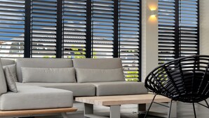 Uma sala de estar moderna com um sofá modular cinza, uma mesa de centro de madeira e uma cadeira preta trançada.