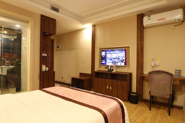 Quarto de hotel com cama, escrivaninha, cadeira, televisão e banheiro com box de vidro.