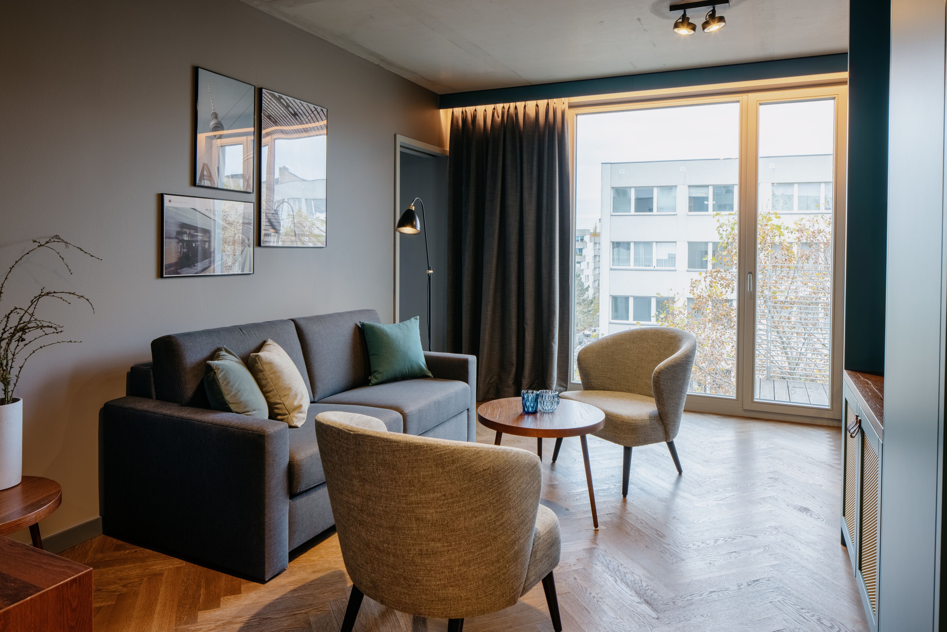 Uma sala de estar moderna com um sofá, duas poltronas, uma mesa de centro e uma janela grande com cortinas.