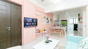 Uma sala de estar moderna com uma TV, uma mesa de centro branca com um vaso, um sofá verde-água e uma cozinha ao fundo.