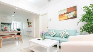 Uma sala de estar moderna com um sofá azul claro, uma mesa de centro branca e uma área de jantar com mobiliário de madeira.