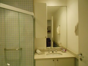 Casa de banho com cabine de duche em vidro, pia com espelho e toalha pendurada na parede.