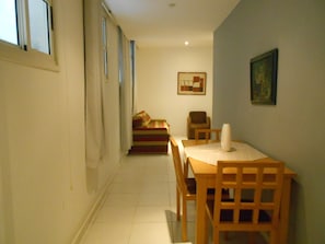 Um corredor com área de jantar, incluindo uma mesa, cadeiras, um sofá e um quadro na parede.
