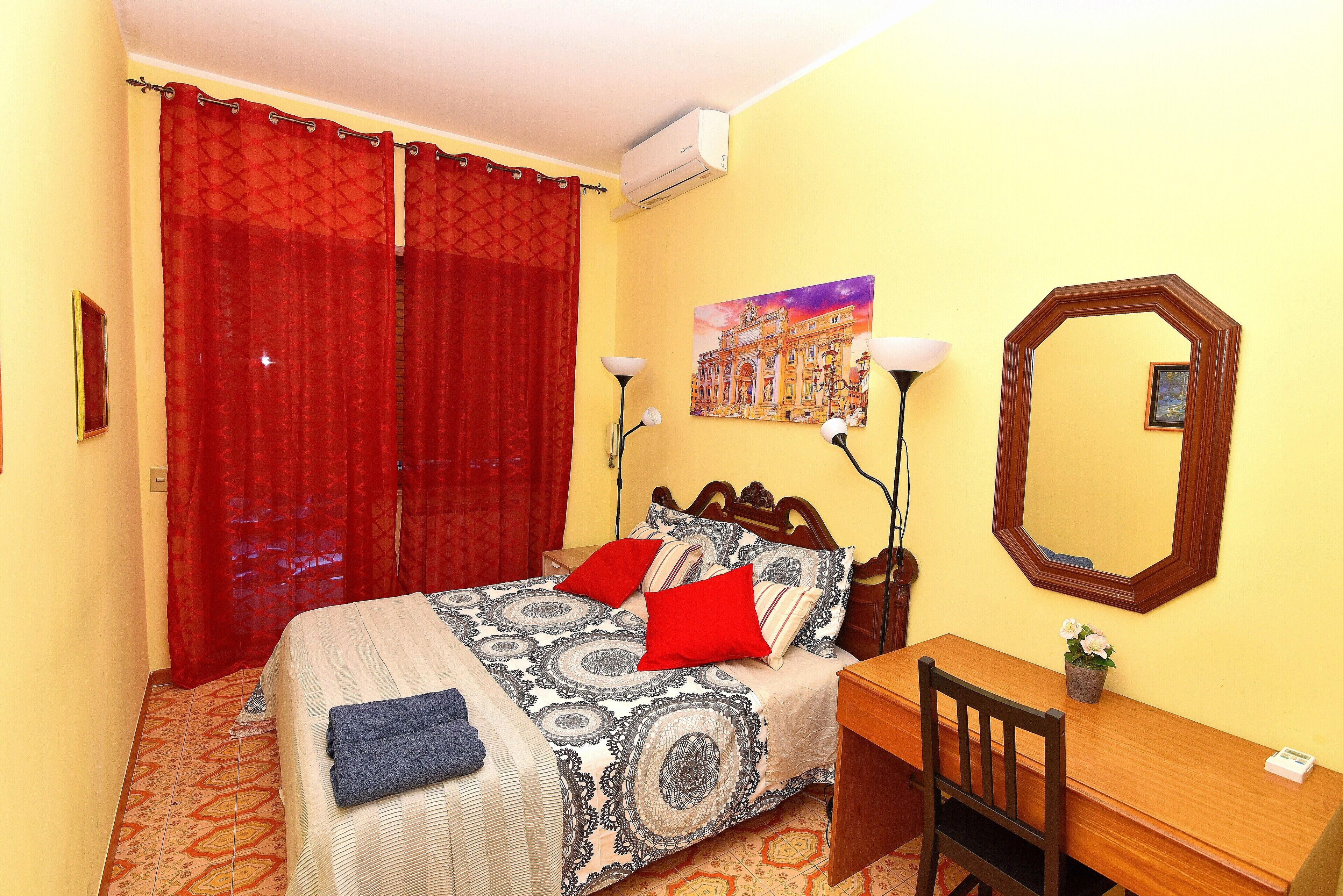 Quarto com cama, escrivaninha, cadeira, espelho e cortina vermelha.