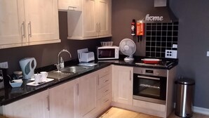 Uma cozinha moderna com armários em tons claros, micro-ondas, torradeira, pia e luminária pendente vermelha.