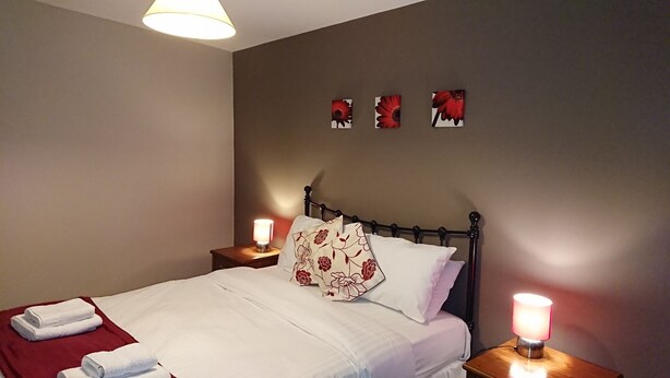 Cama bem arrumada com lençóis brancos, duas luminárias de cabeceira e almofadas estampadas com flores.
