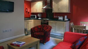 Um espaço de estar compacto com cozinha, área de jantar e sala de estar com sofá vermelho e mesa de madeira.