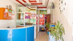 Uma área de recepção de hotel com balcão azul, certificados emoldurados e um relógio na parede.