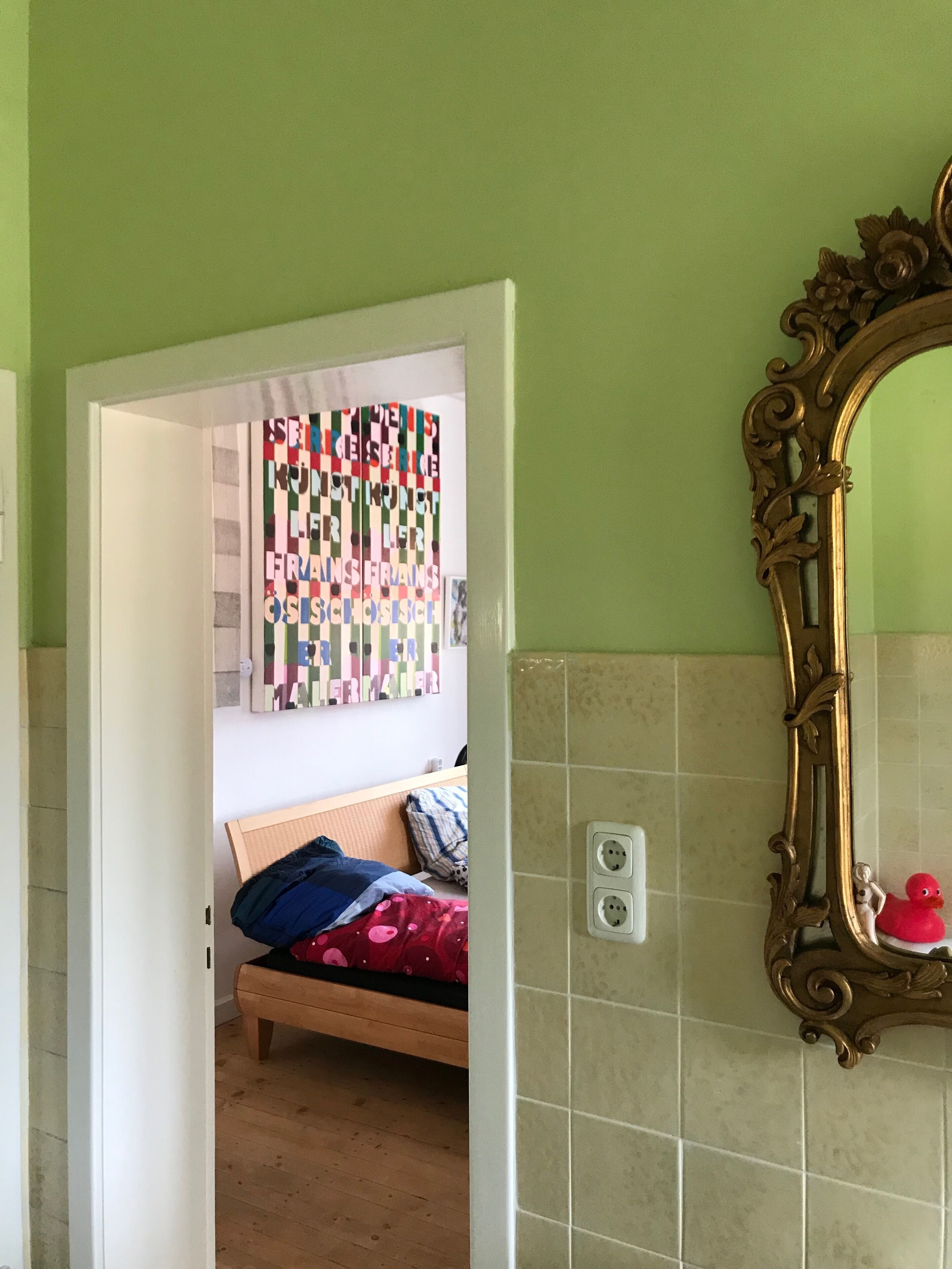 Um quarto com cama, espelho fixado na parede e um edredom colorido na parede.