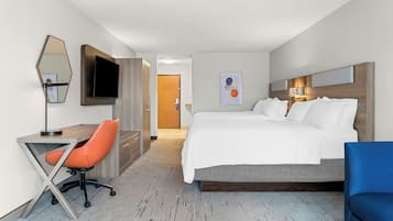 Quarto de hotel com cama, escrivaninha com cadeira, televisão e espelho.