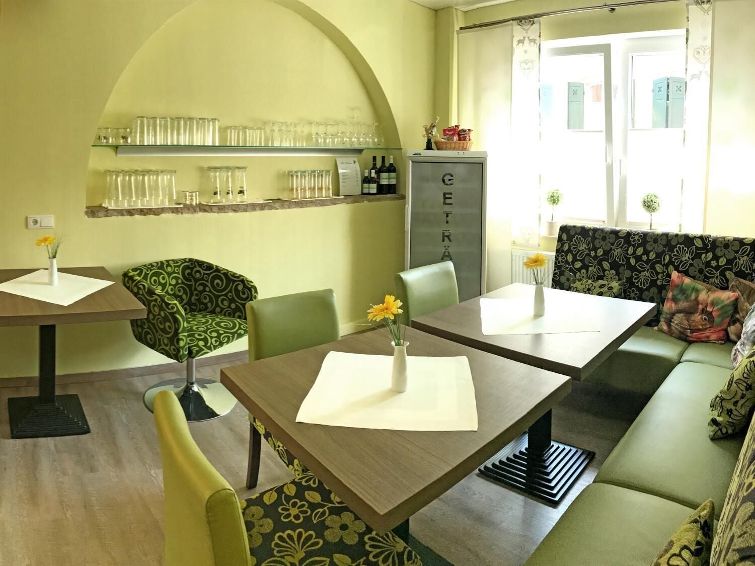 Uma sala de jantar com mesas, cadeiras, um sofá e uma geladeira com uma garrafa de vinho.