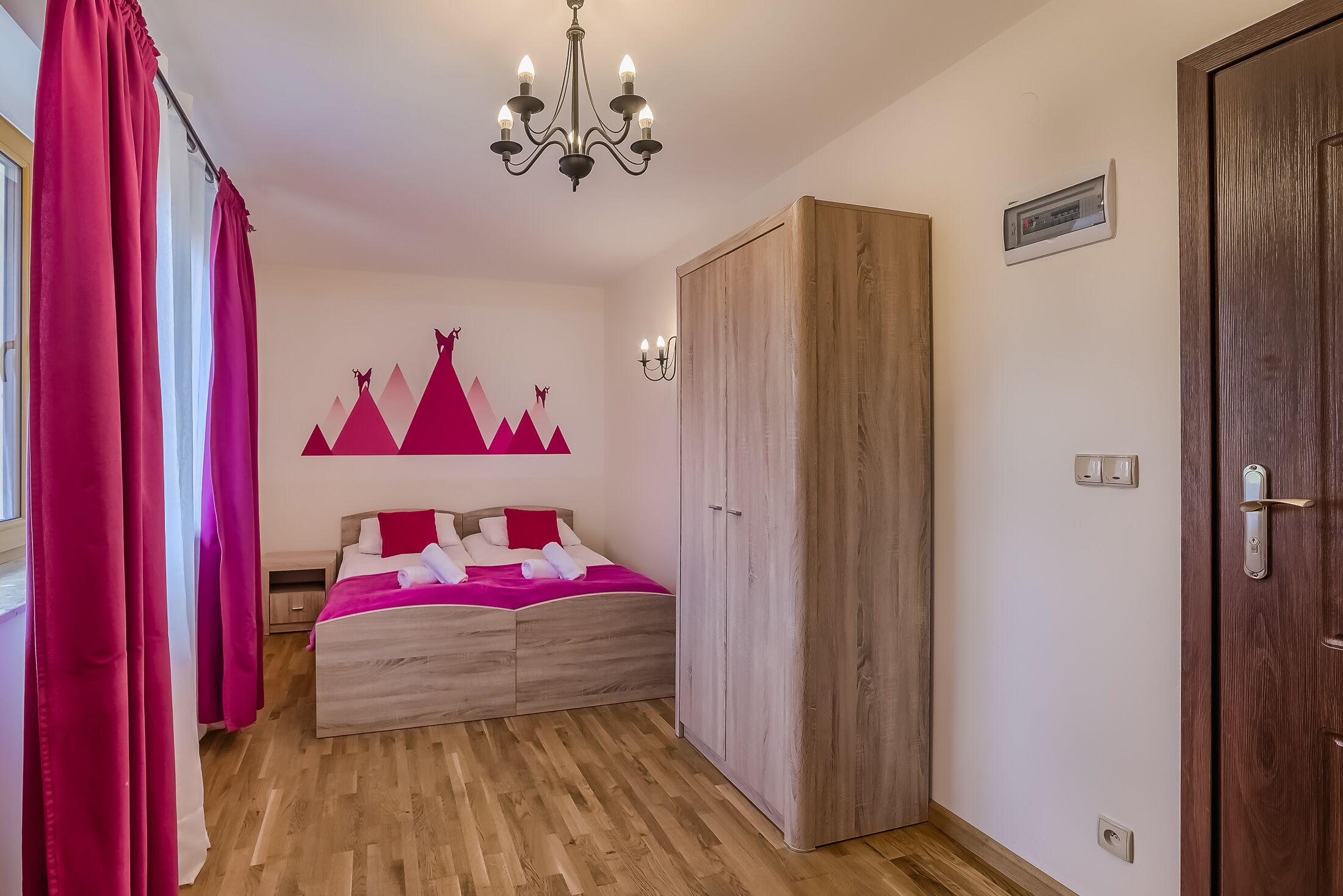 Quarto com cama de madeira, guarda-roupa, candelabro e parede com desenho de montanhas.