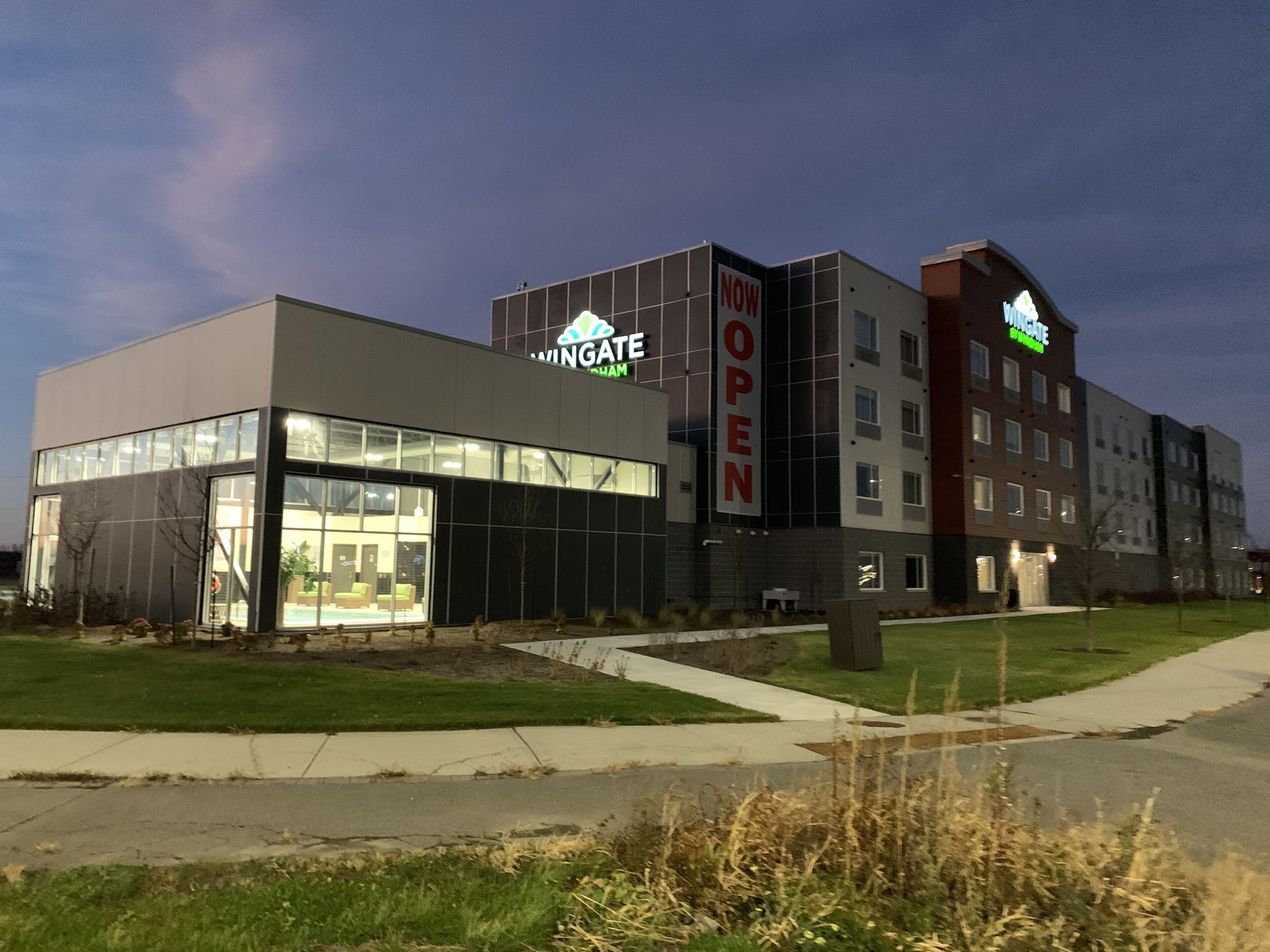 Um hotel moderno com fachada de vidro, um sinal chamativo com a palavra 'OPEN' e um terraço no telhado.