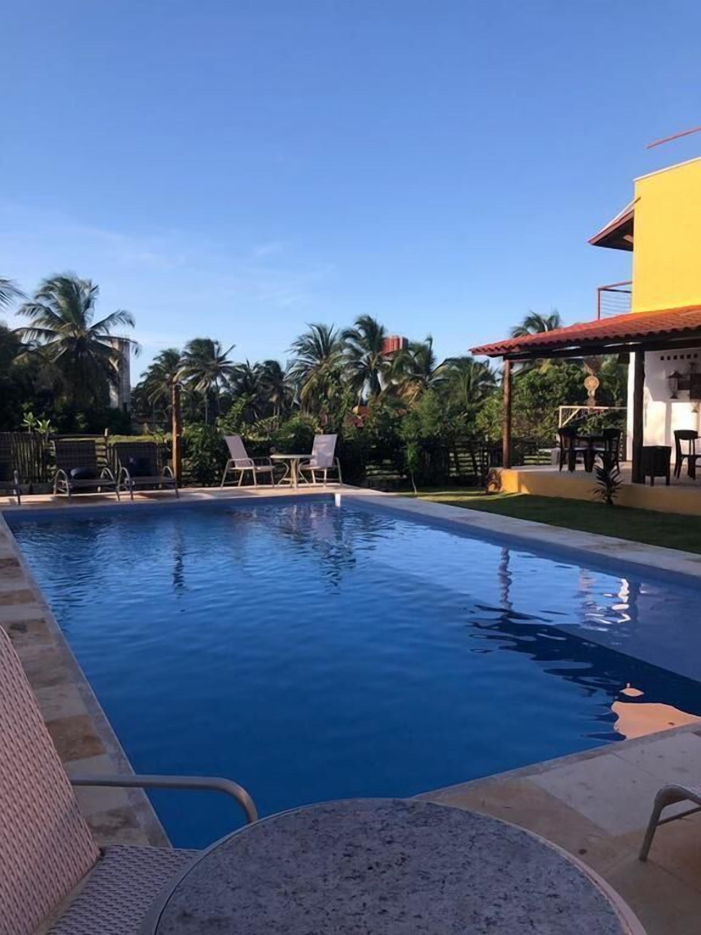 Uma piscina com espreguiçadeiras e uma área coberta com mesas e cadeiras.