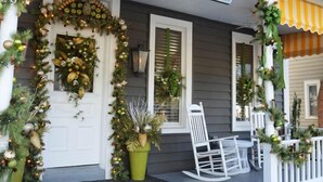 Varanda decorada com guirlandas e enfeites de Natal, uma cadeira de balanço branca e uma chaminé de tijolos.