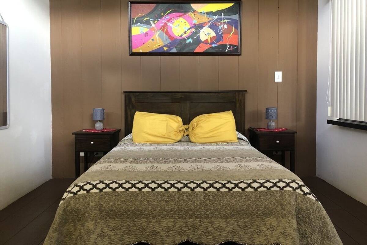 Quarto de hotel com cama grande, duas mesas de cabeceira, televisão fixada na parede e janela com persianas.