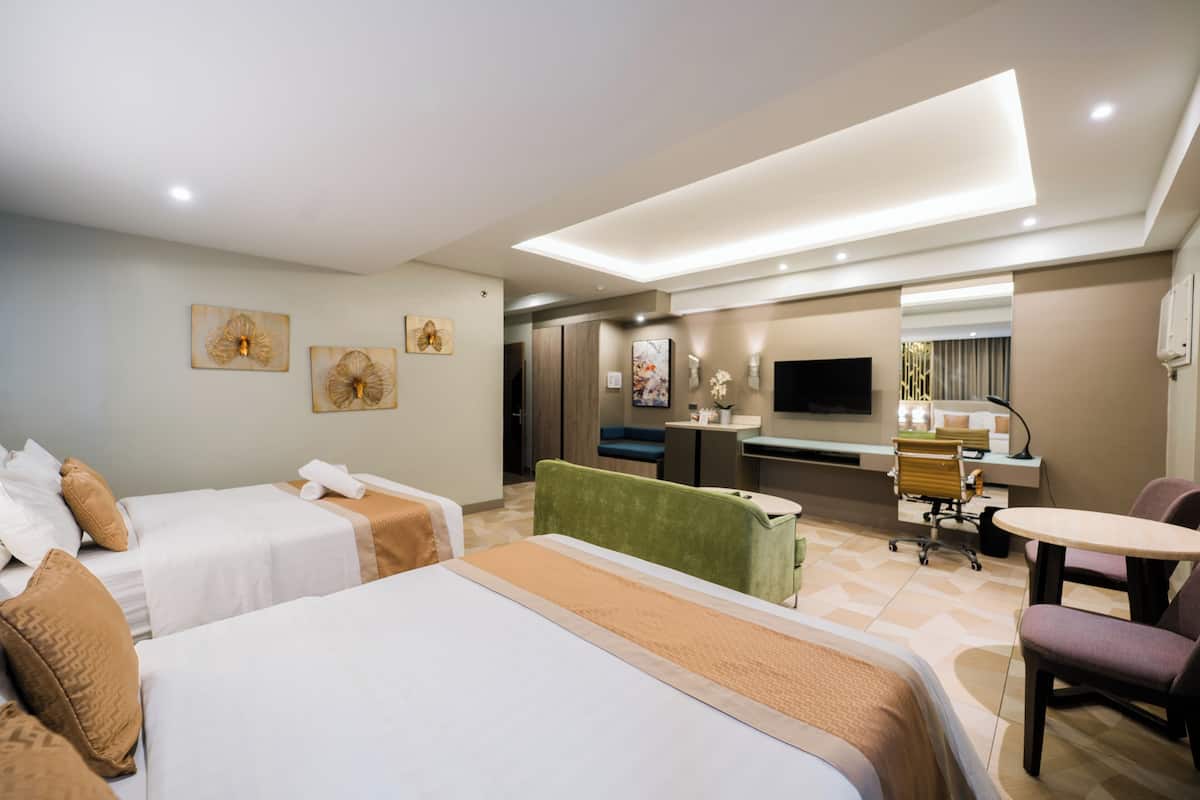 Quarto de hotel com duas camas, uma escrivaninha, uma cadeira e uma televisão.