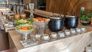 Buffet com diversos alimentos e bebidas, incluindo salada, frutas e pratos quentes.