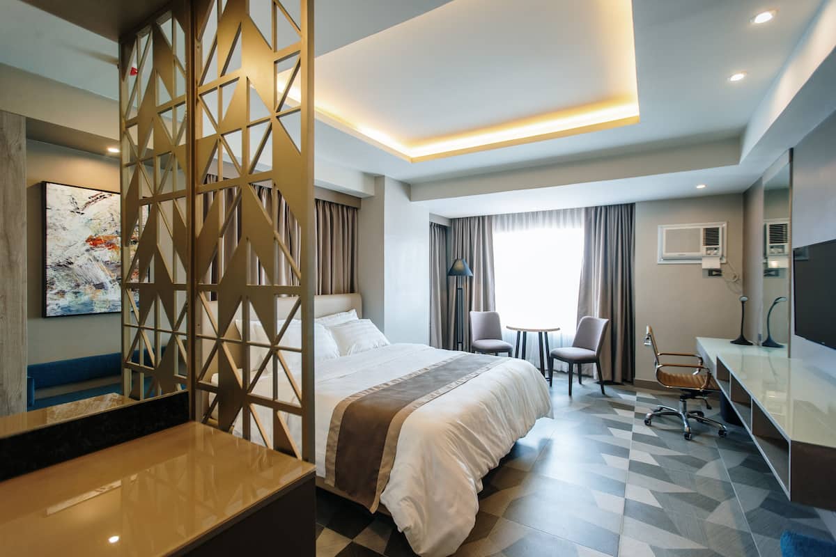 Quarto de hotel com uma cama grande, uma escrivaninha, uma cadeira e uma televisão.