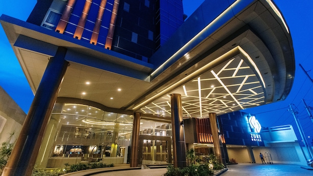 Uma entrada de hotel moderna com fachada curva, grandes janelas de vidro e um letreiro chamativo.