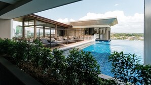 Uma área moderna de piscina ao ar livre com espreguiçadeiras e um bar, cercada por vegetação.