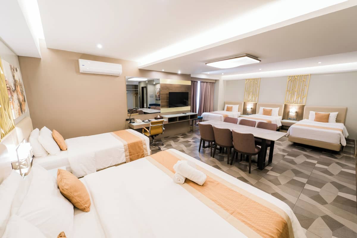 Quarto de hotel com duas camas, uma escrivaninha, uma cadeira, uma televisão e um espaço de refeições.