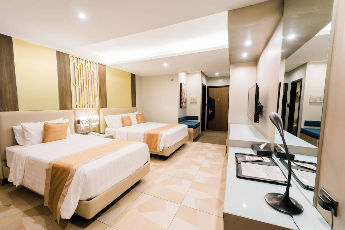 Quarto de hotel com duas camas, uma escrivaninha com computador e um espelho.