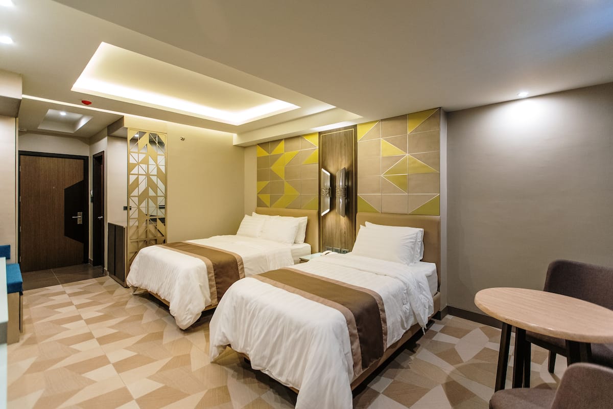 Quarto de hotel com duas camas, uma mesa pequena e uma cadeira.