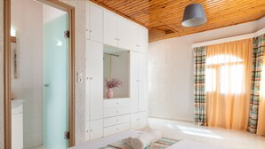 Quarto com cama, roupeiro espaçoso, cabine de chuveiro em vidro e janela com cortinas.