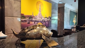 Bancada de recepção com uma grande escultura de peixe, uma parede de mármore e um pôster de uma paisagem urbana.